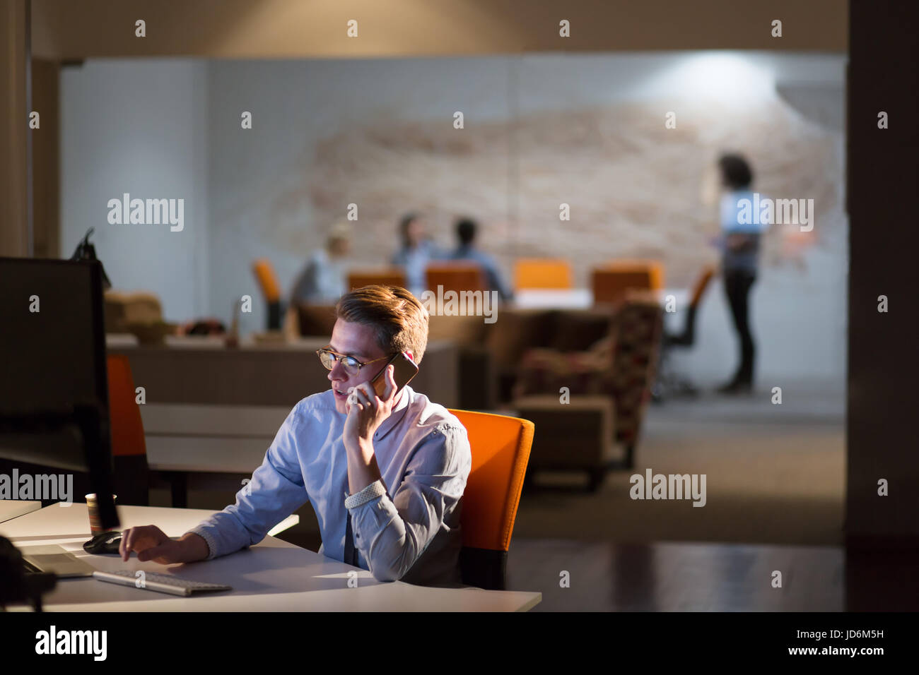 Young man using mobile phone while working on computer at night in dark ...