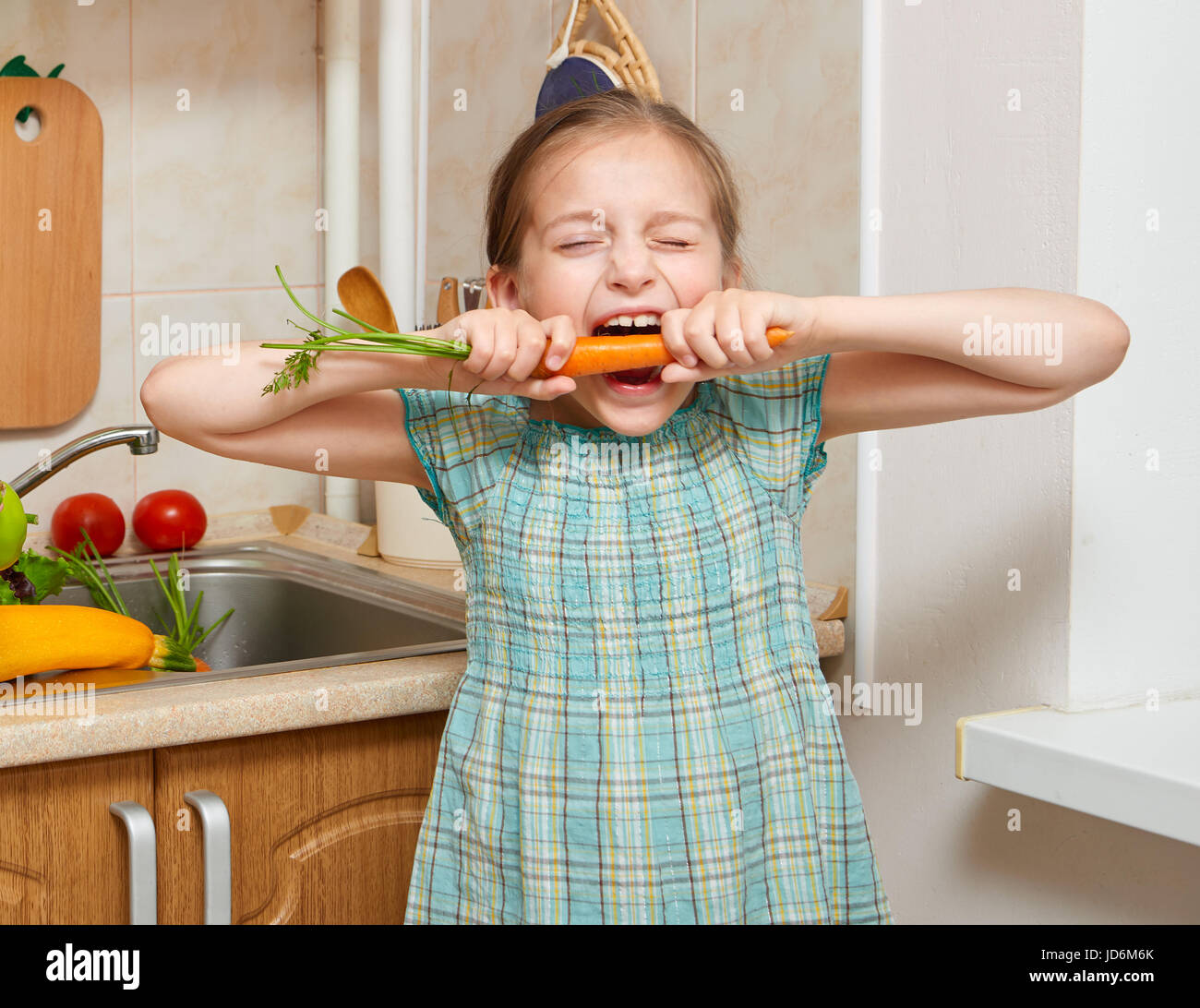 child girl eat carrot, vegetables and fresh fruits in kitchen interior ...