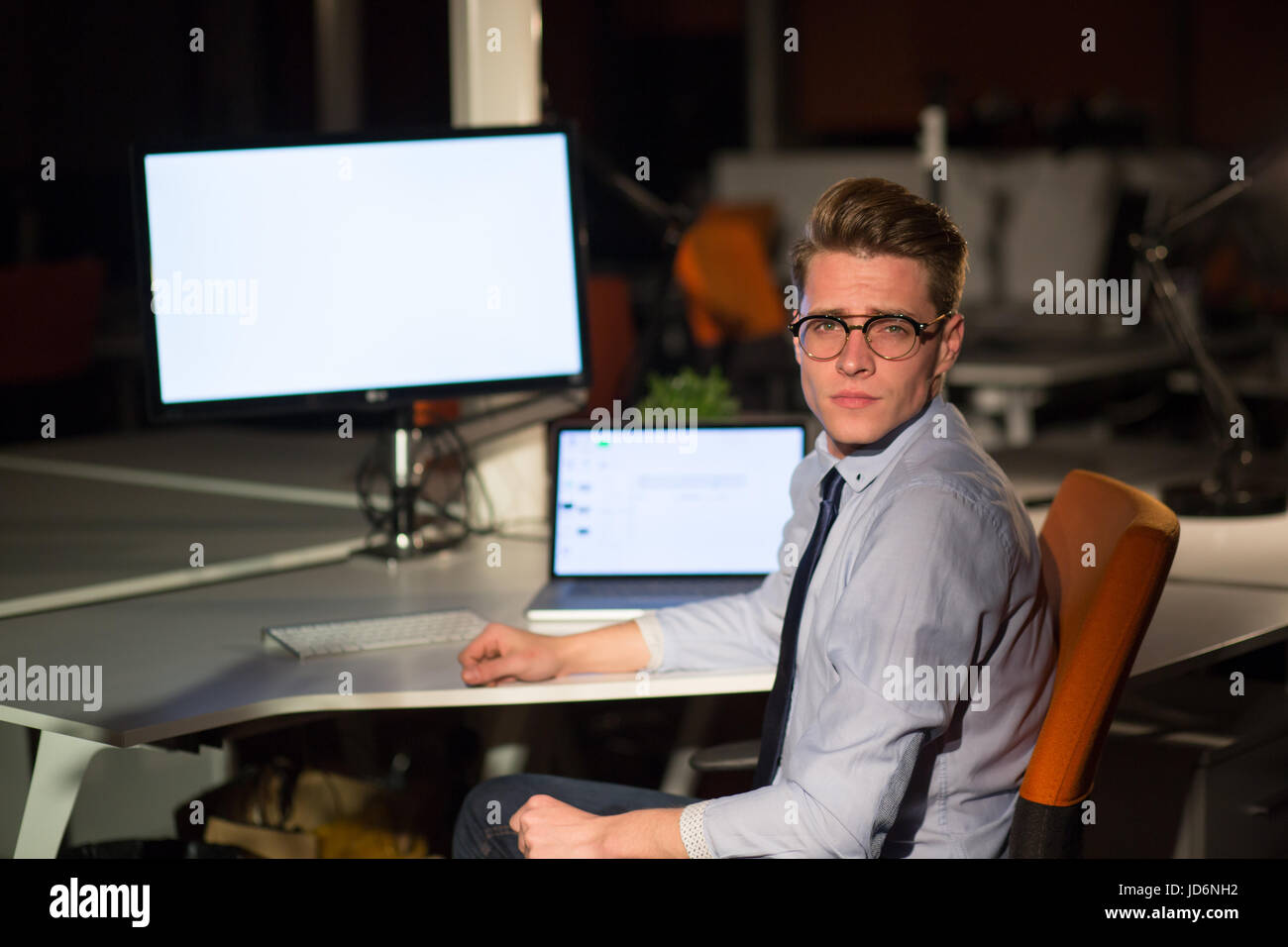 Young man working on computer at night in dark office. The designer ...