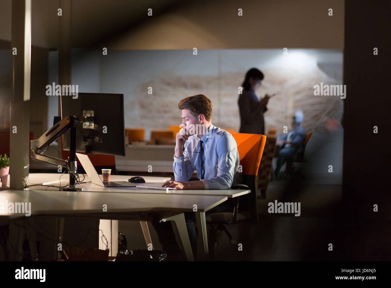 Young man working on computer at night in dark office. The designer ...