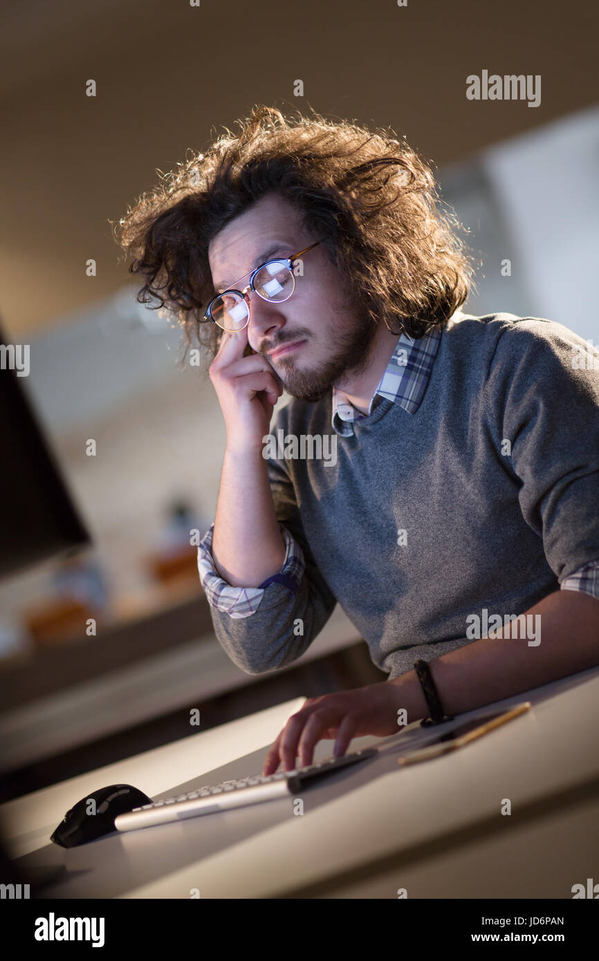 Young man working on computer at night in dark office. The designer ...