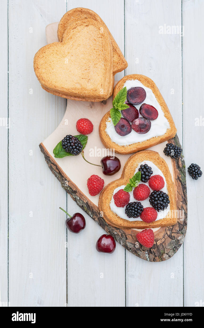 Heart shaped biscuits spread with quark, cherries and a twig of mint ...