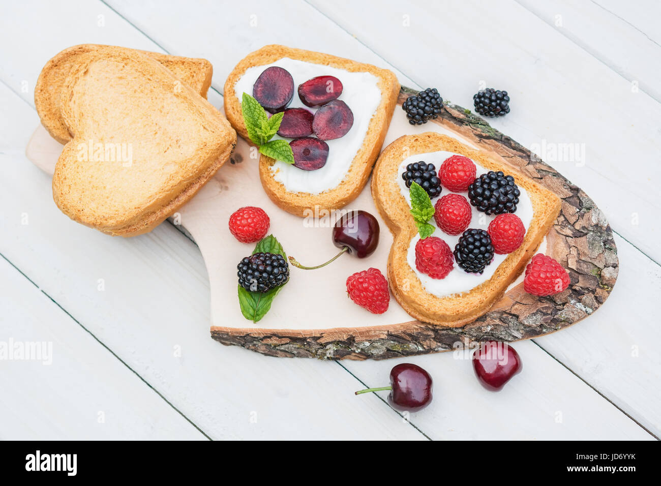 Heart shaped biscuits spread with quark, cherries and a twig of mint ...