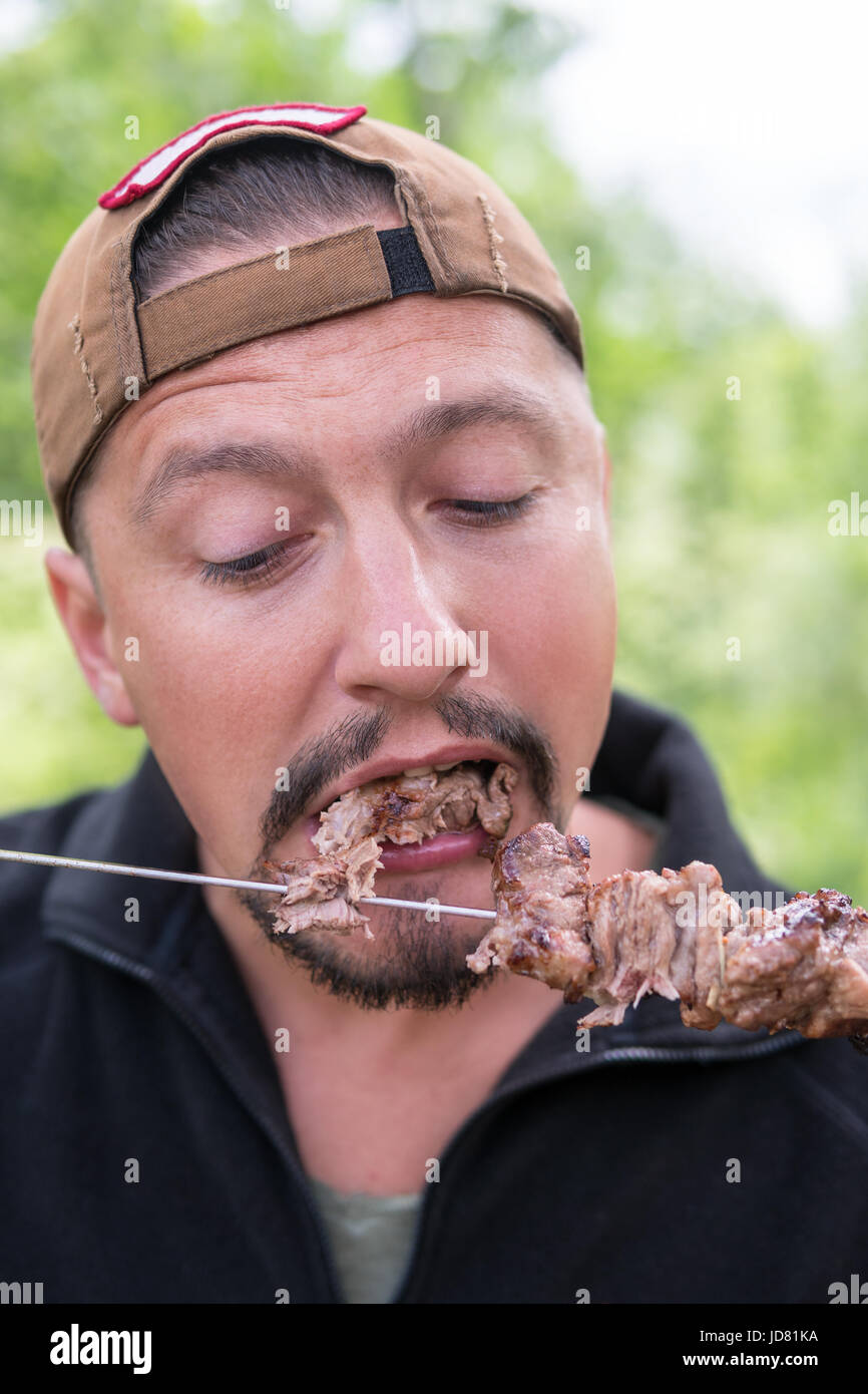Bearded man eats a shish kebab tearing him from the skewer with his ...