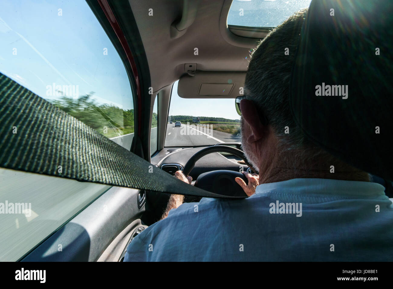 Rear view of man driving car, view over shoulder with seat belt ...