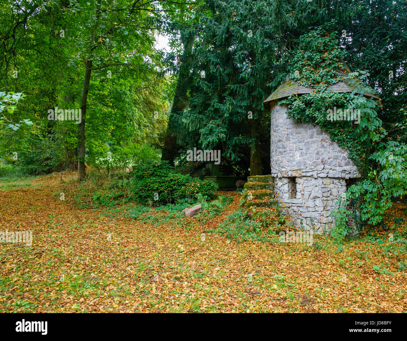Small round stone building with trees and autumn leaves on ground ...