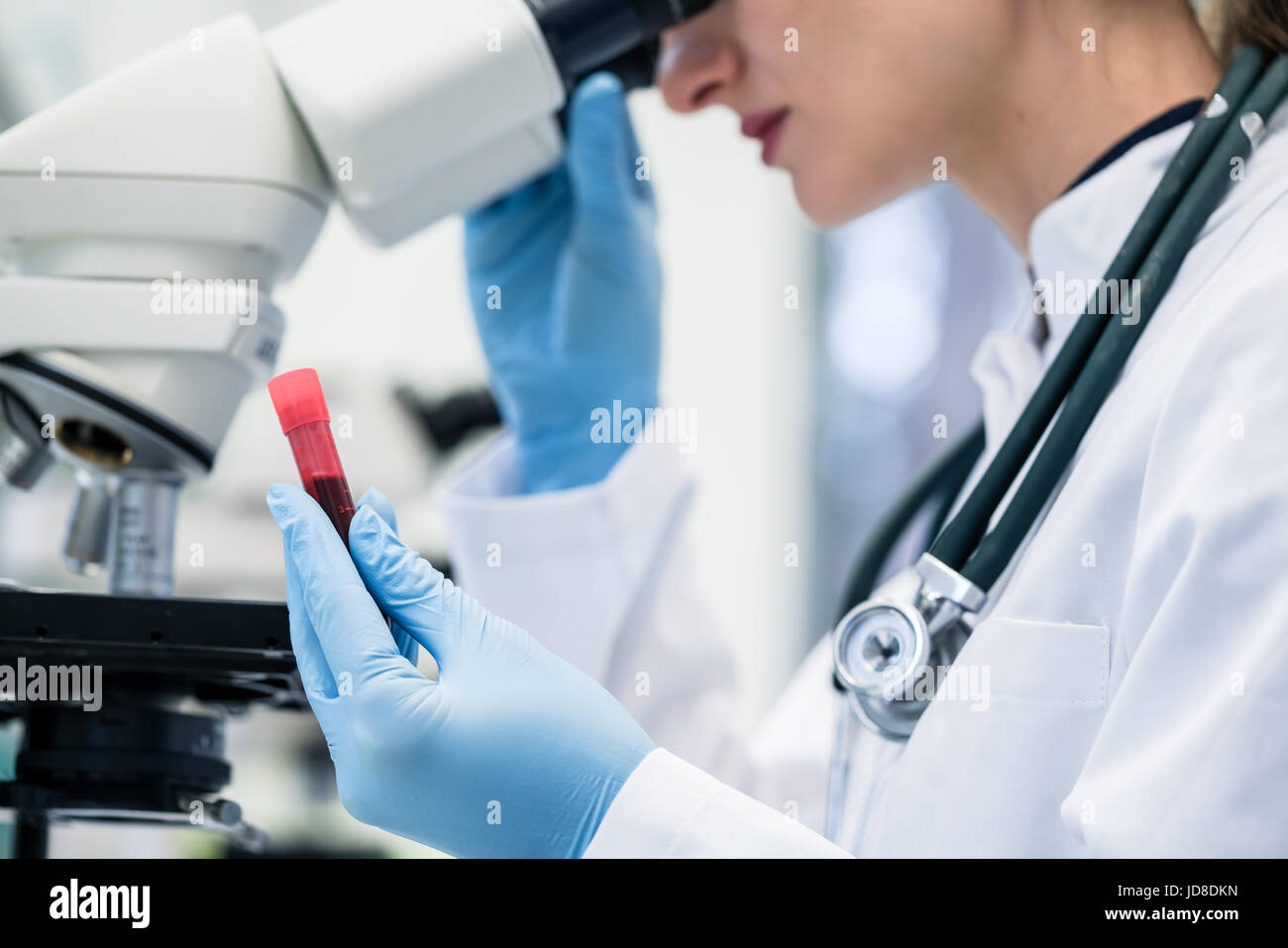 Woman examining blood sample under microscope in medical or scientific ...