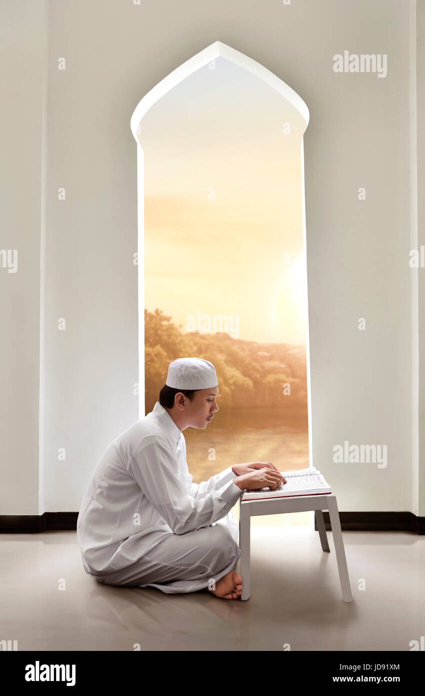 Young asian muslim man with cap reading holy book Koran on the mosque ...