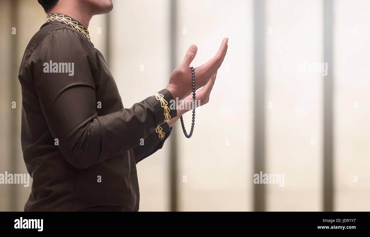 Muslim man raising hand and praying with prayer beads on the mosque ...