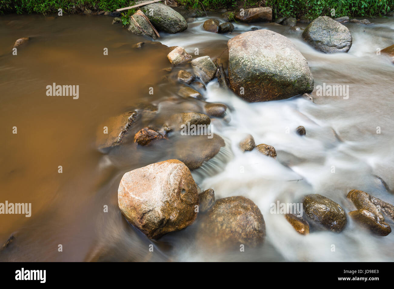 Scenery of brown watercourse with flowing water and white wave on rock ...