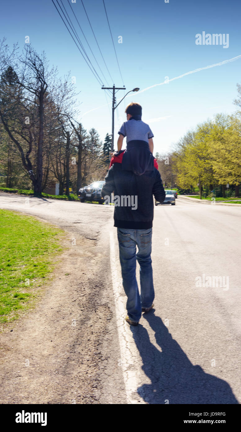 Man walking along road carrying boy on shoulders in sunshine Stock ...