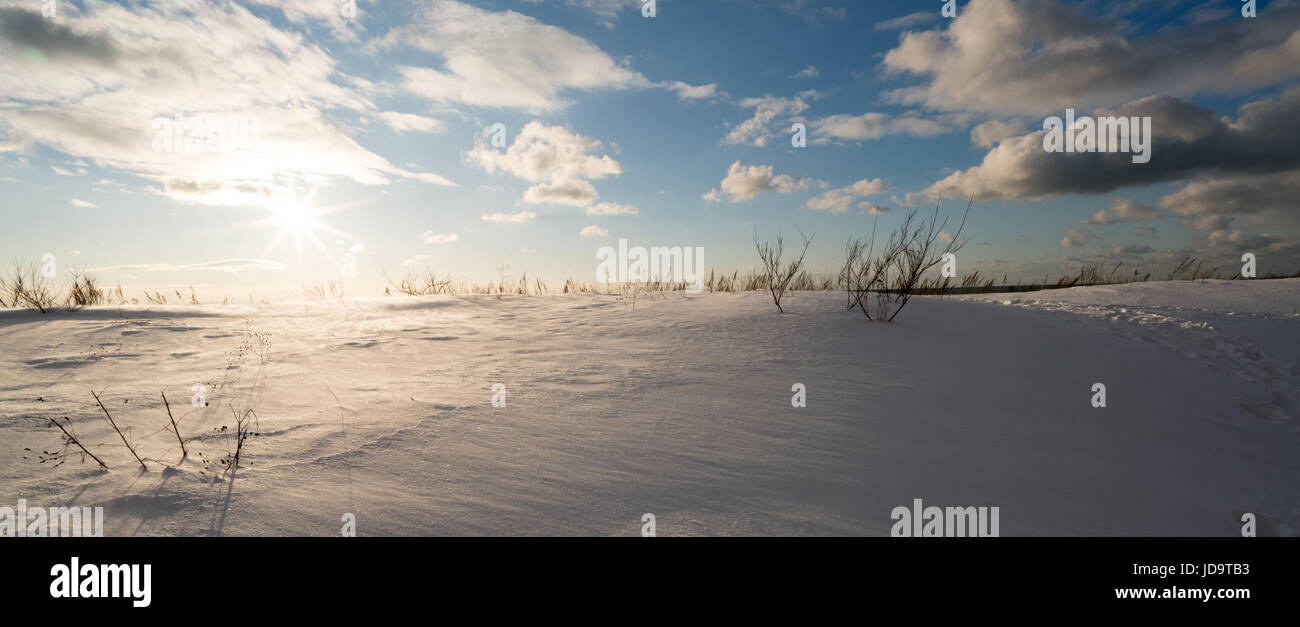 Snow covered rural landscape with bright sunlight and fluffy clouds in ...