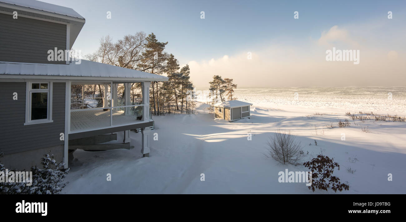 House and cabin in snow covered landscape, sun casting shadow in snow ...
