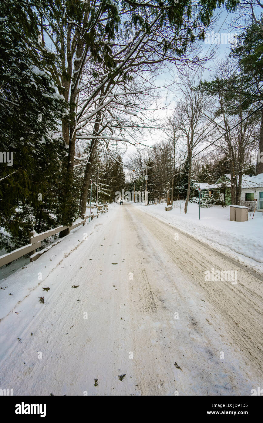 Snow covered rural road, two people walking in distance, residential ...