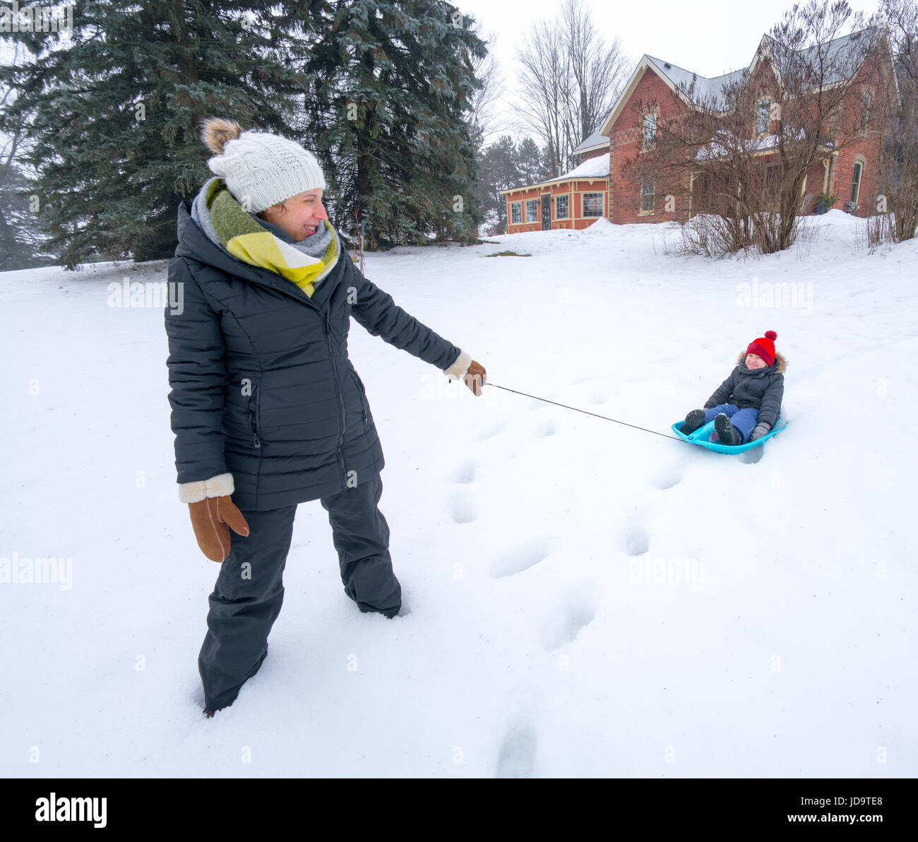 Outdoors at day, mother pulling son on sledge in snow, Ontario, Canada ...