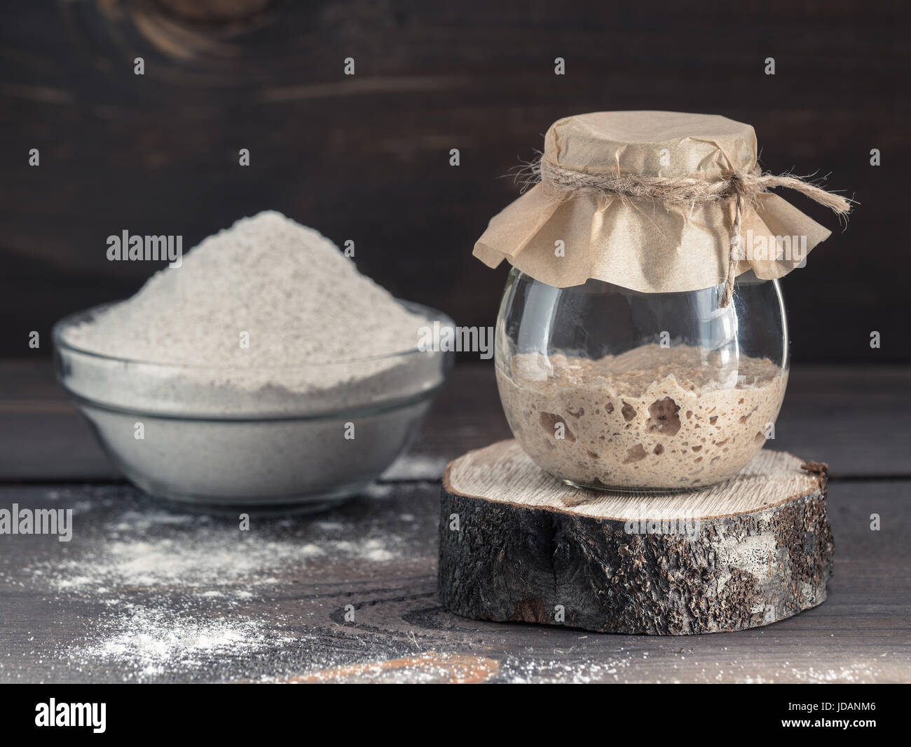Active rye sourdough starter in glass jar and rye flour on brown wooden ...
