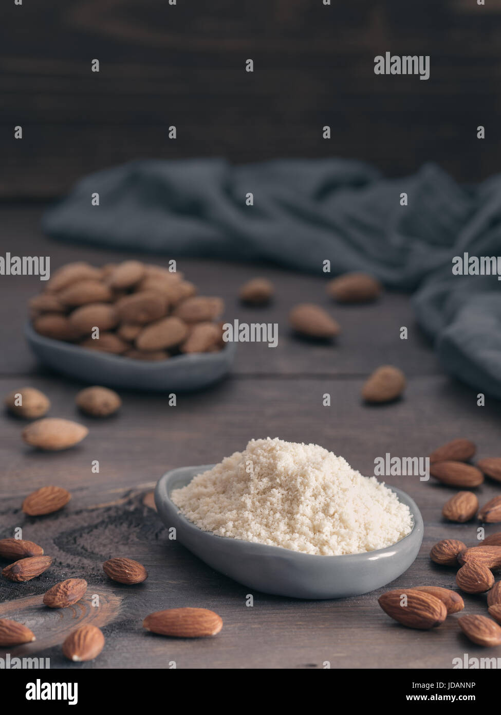Almond powder in gray trendy plate and almonds on dark wooden table ...