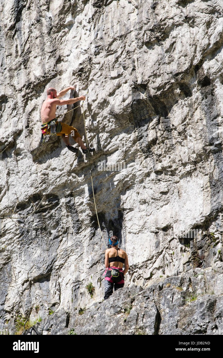 Male and female rock climbers climbing on limestone rockface at Malham ...