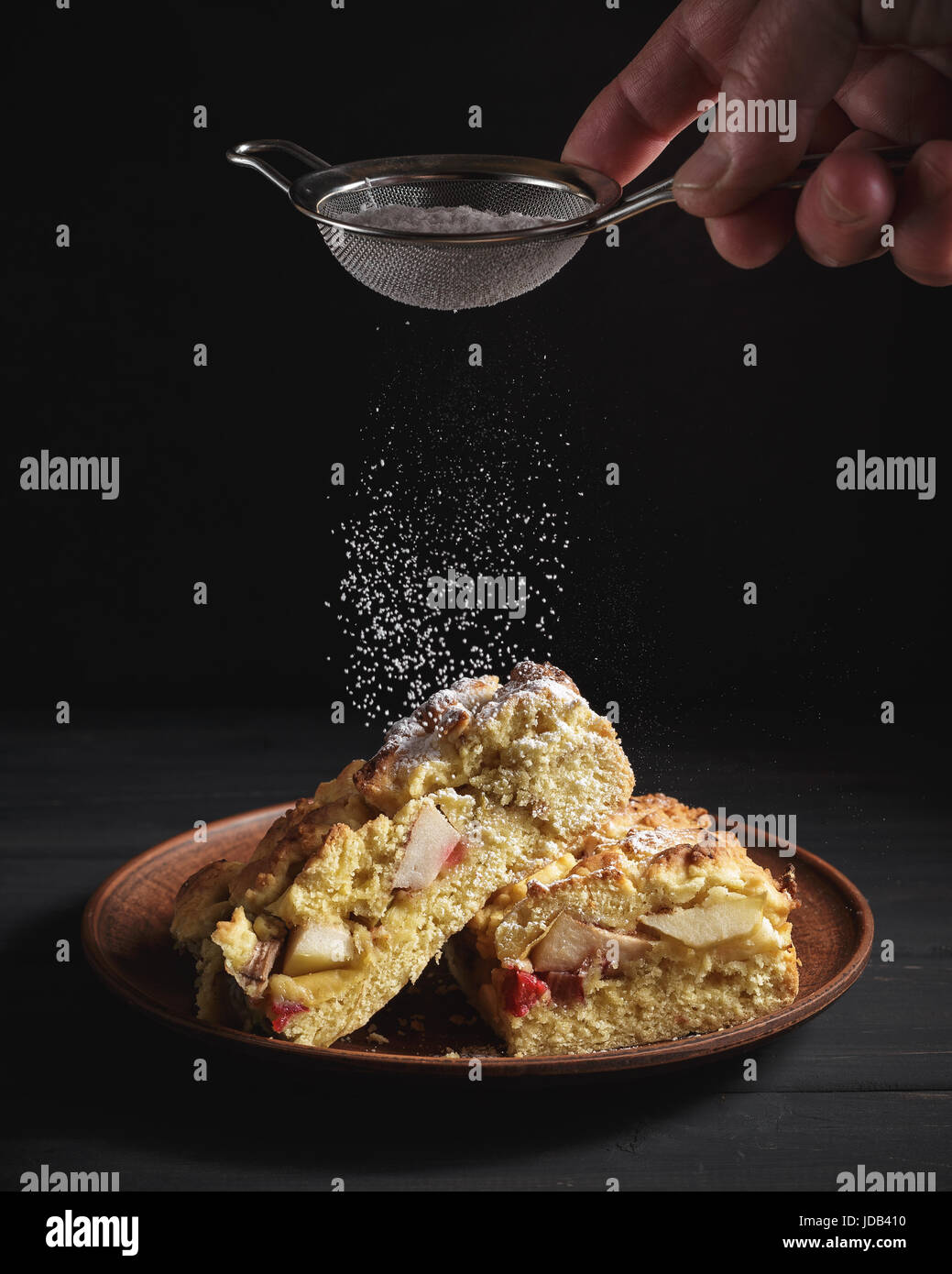Pouring sugar powder on two pieces of pie on brown clay plate over ...
