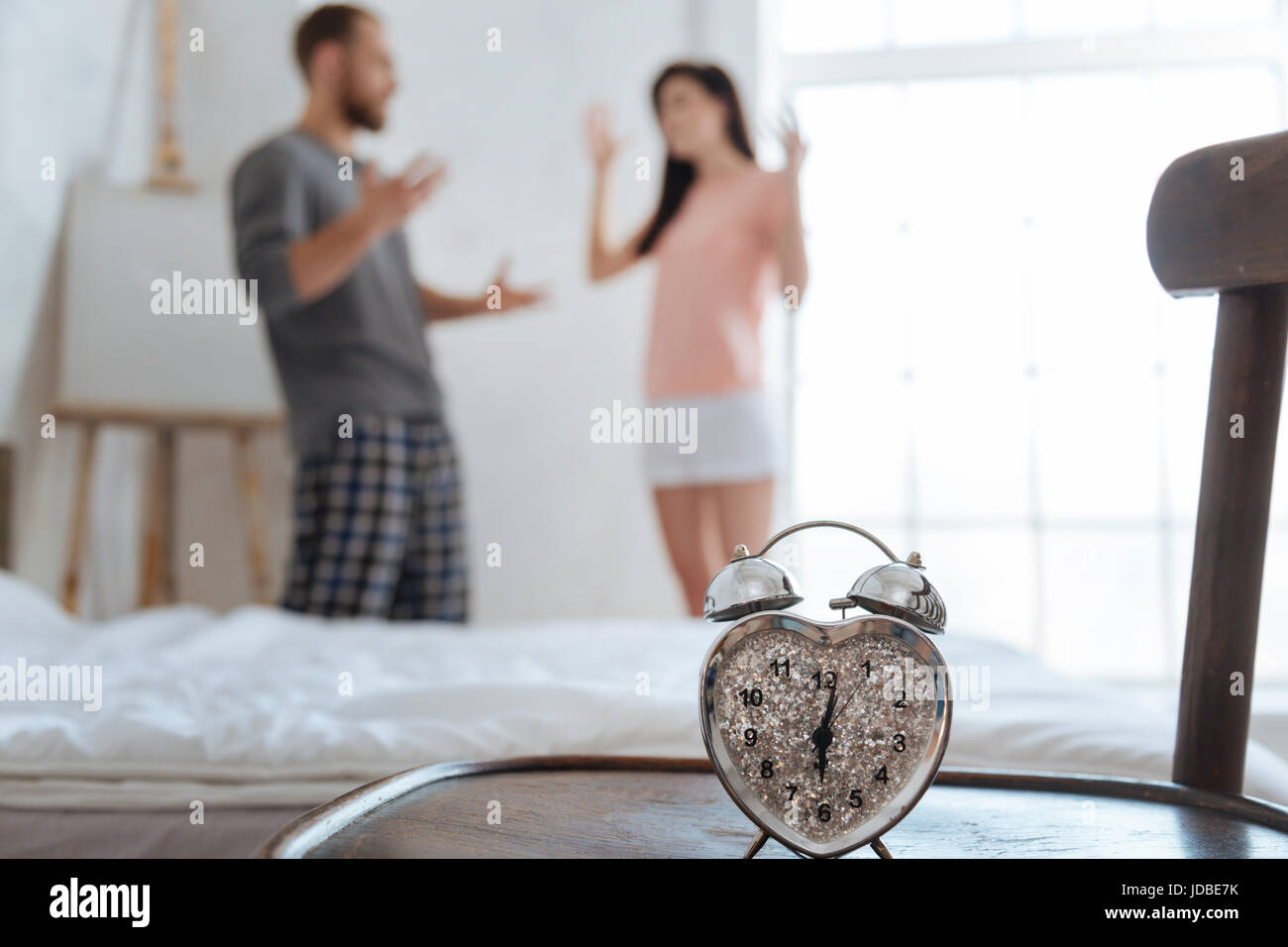 Selective focus on alarm clock with emotional couple on background ...