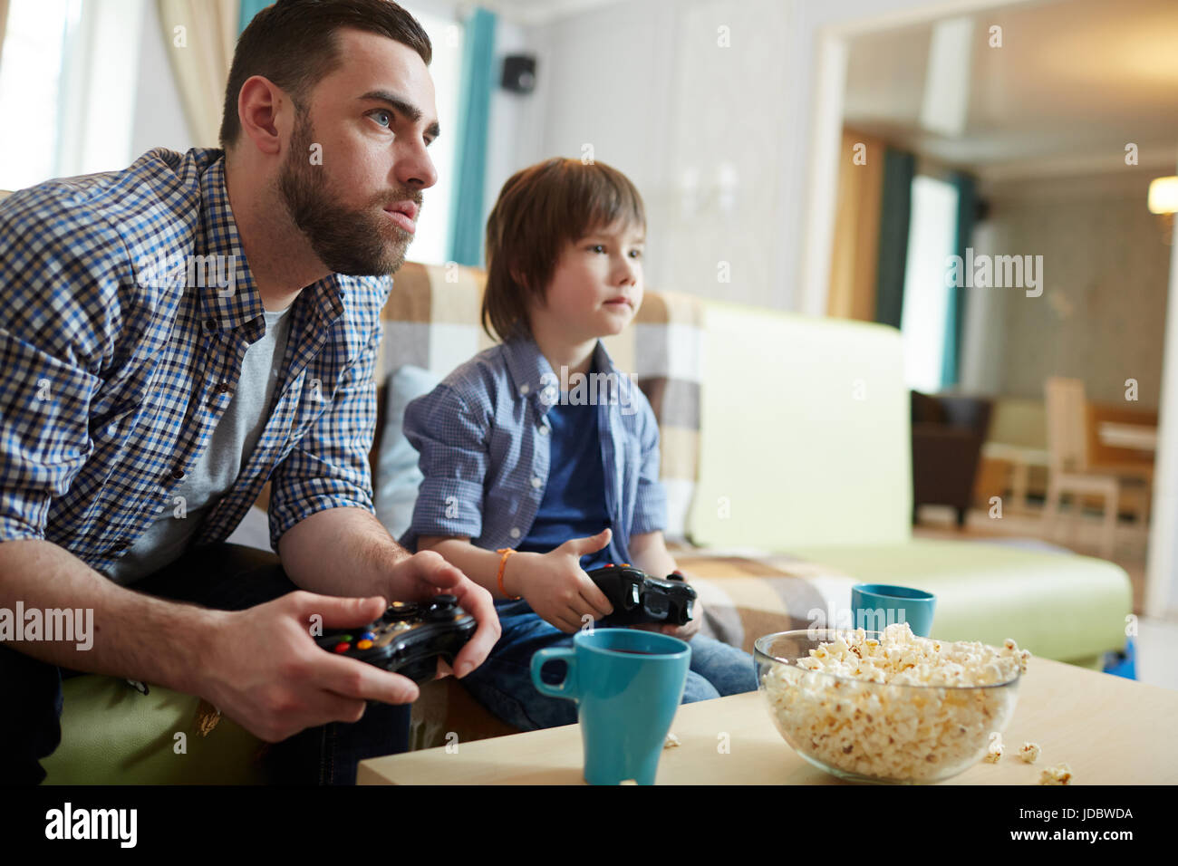 Serious man and little boy with consoles watching and playing video ...
