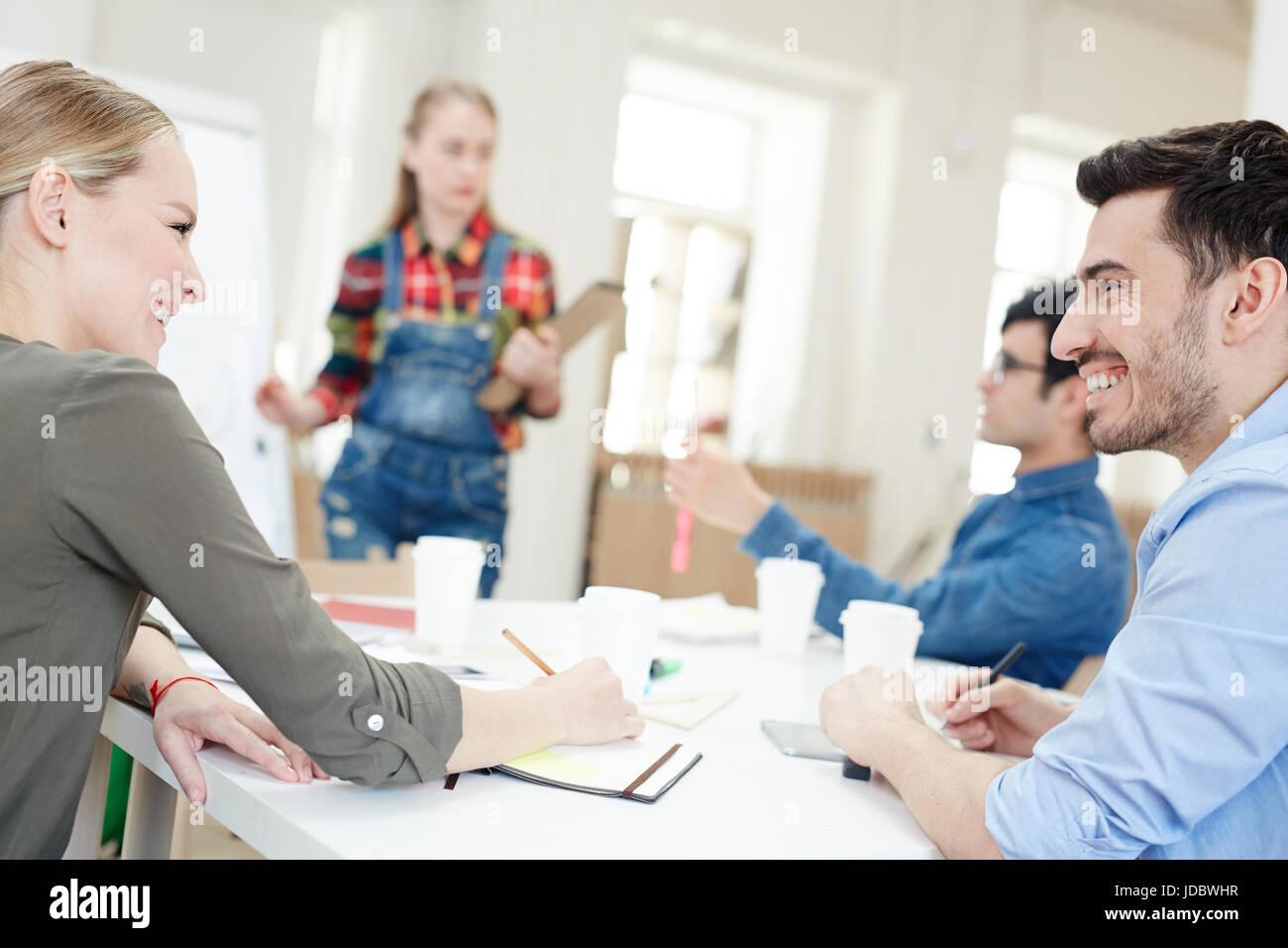 Happy groupmates discussing task by workplace Stock Photo - Alamy