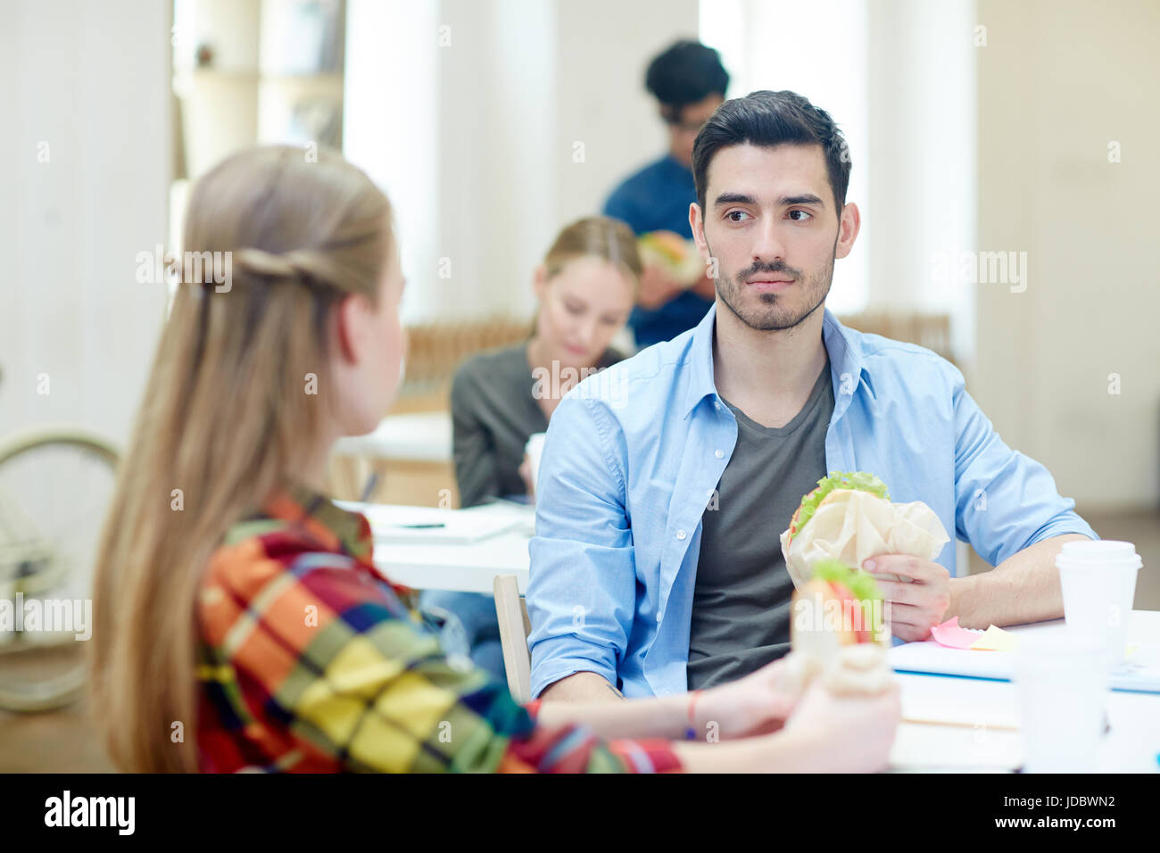Serious guy with sandwich talking to groupmate during lunch break Stock ...