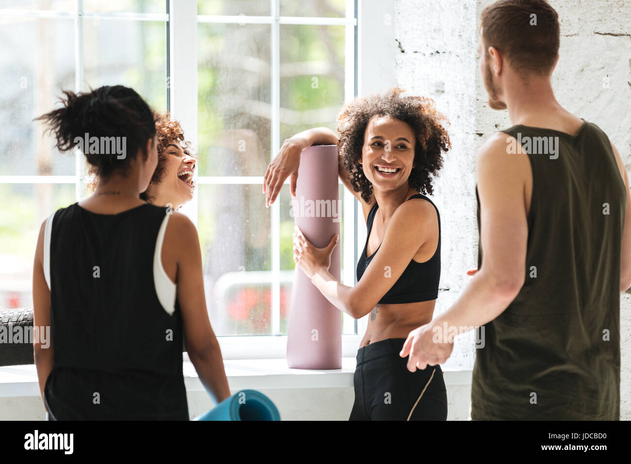 Smiling african woman talking with friends while doing yoga in gym ...