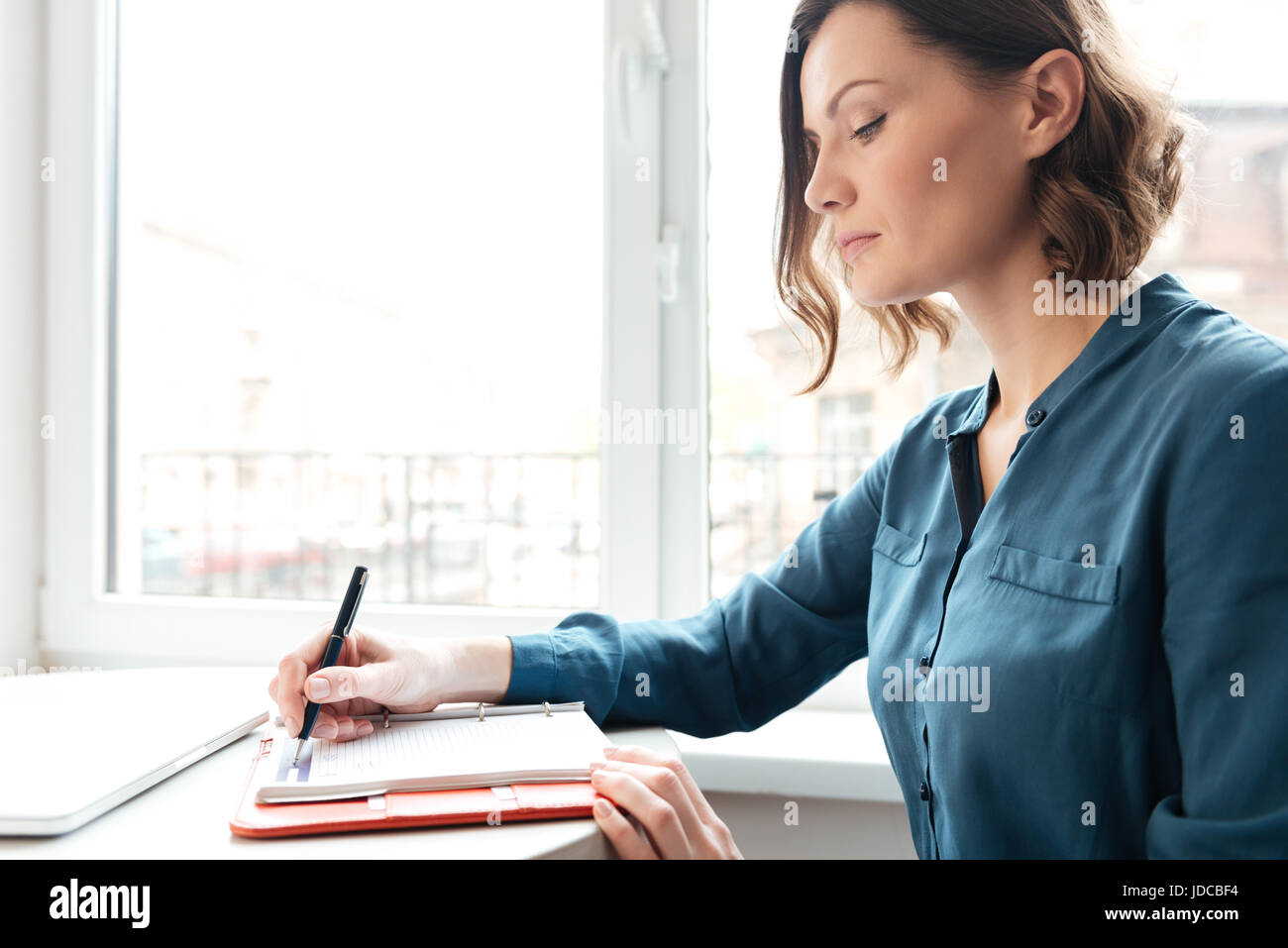 Side view of a young woman making notes in her diary while sitting ...
