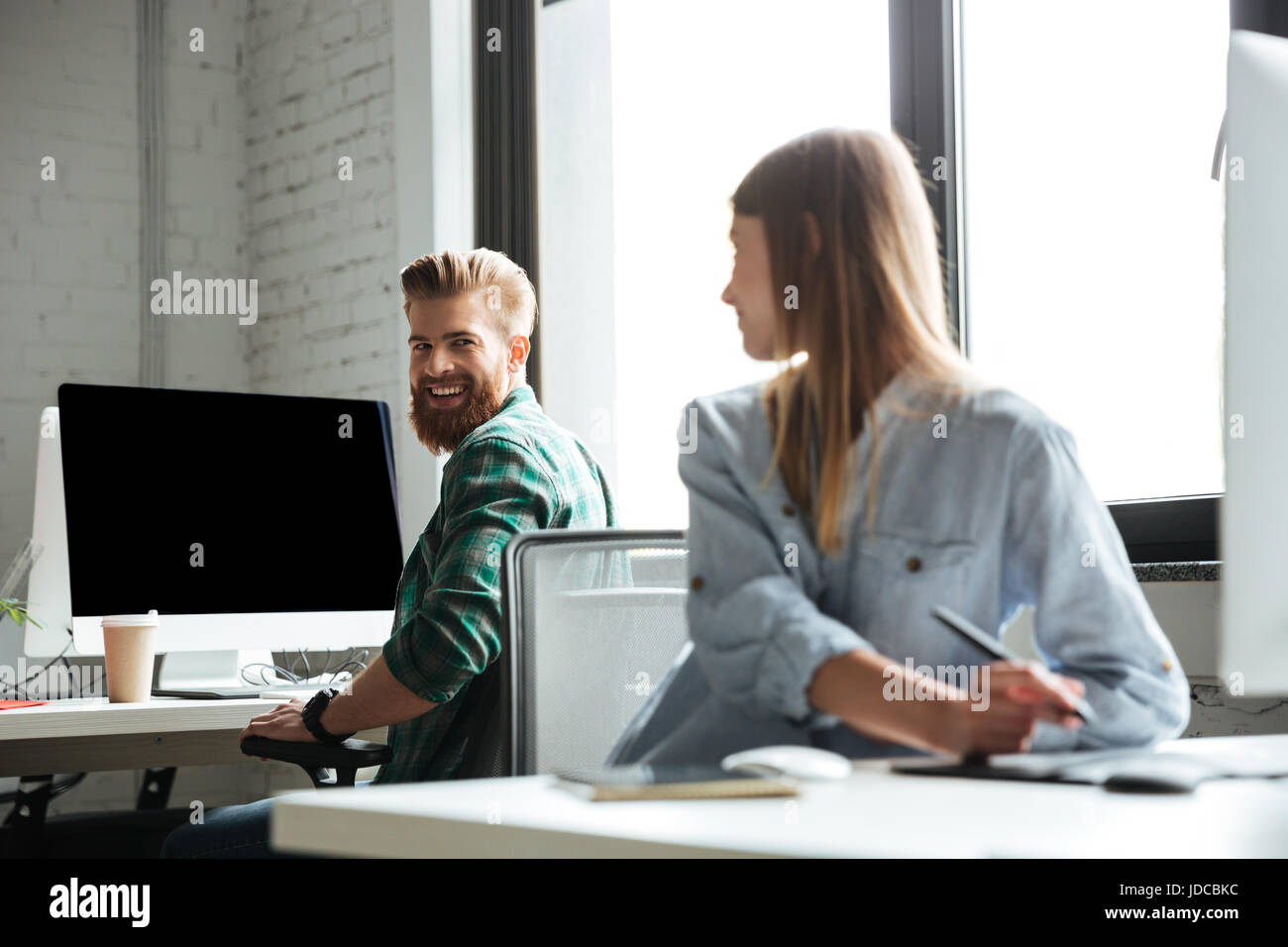 Image of two young happy colleagues work in office using computers ...