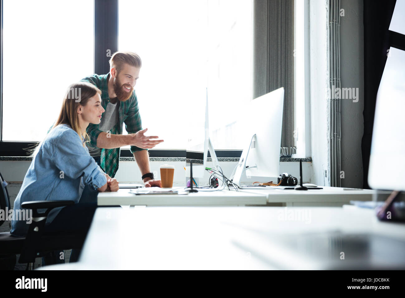 Image of two young smiling colleagues work in office using computers ...