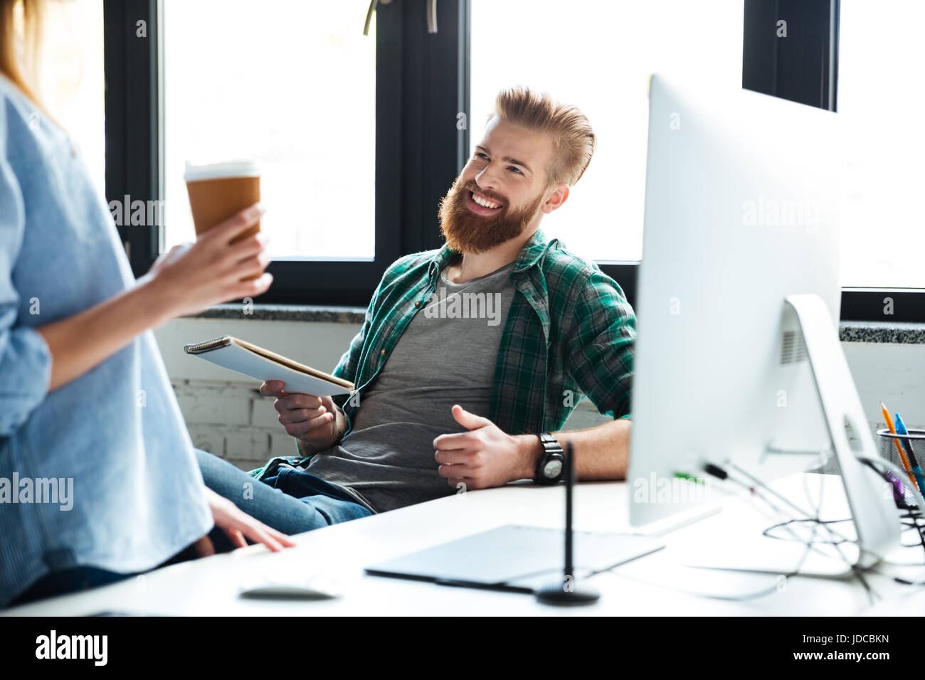 Picture of two young smiling colleagues work in office using computers. Looking aside. Focus on ...