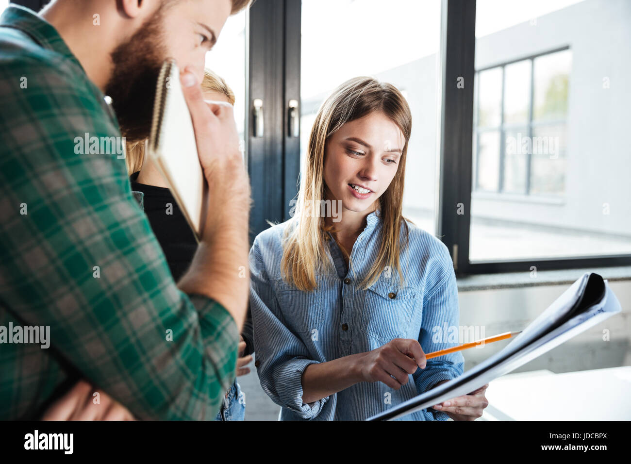 Image of young colleagues in office talking with each other holding ...
