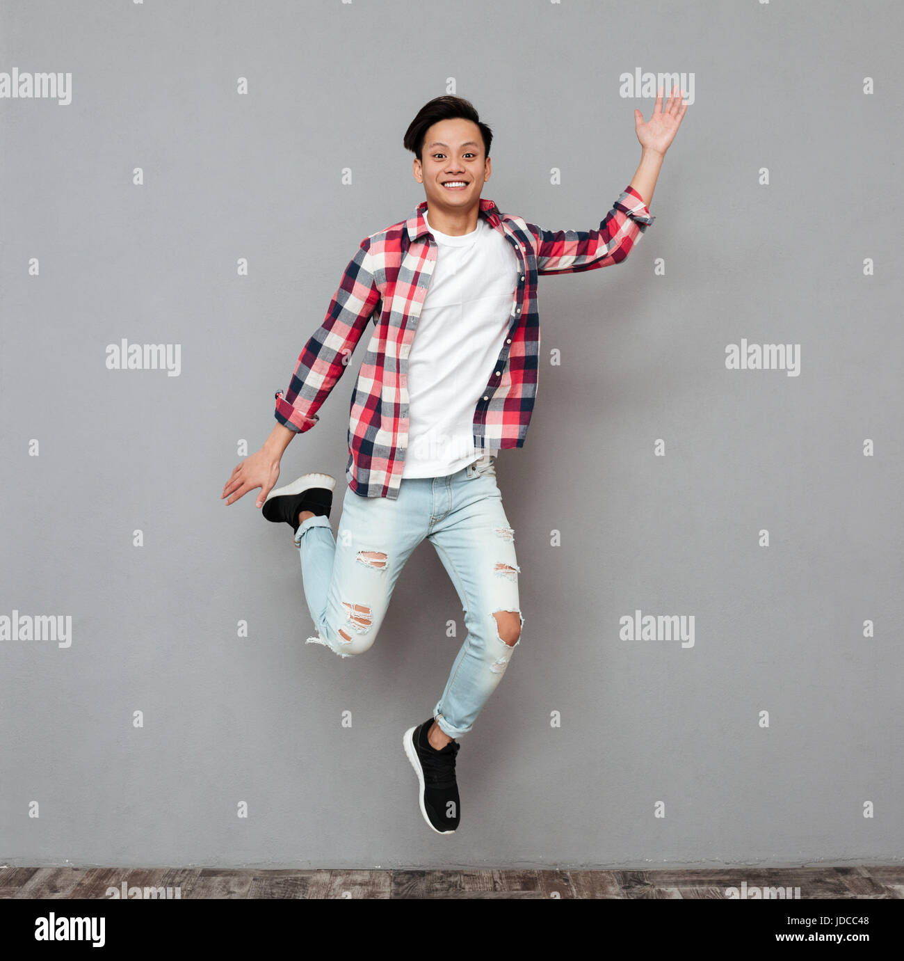 Picture of jumping young asian man over grey background. Looking at ...