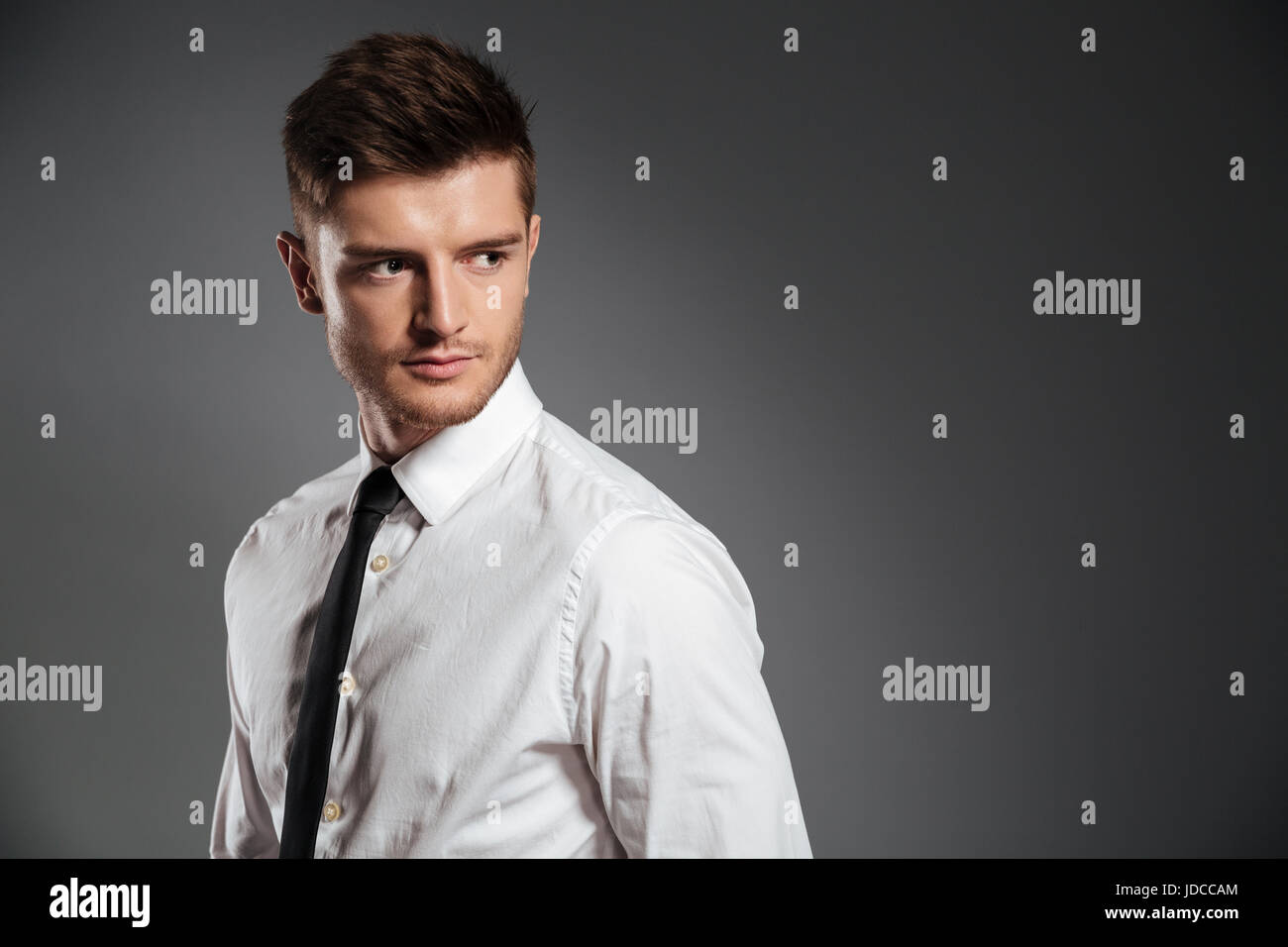 Serious handsome man in shirt and tie standing and looking away at copy ...