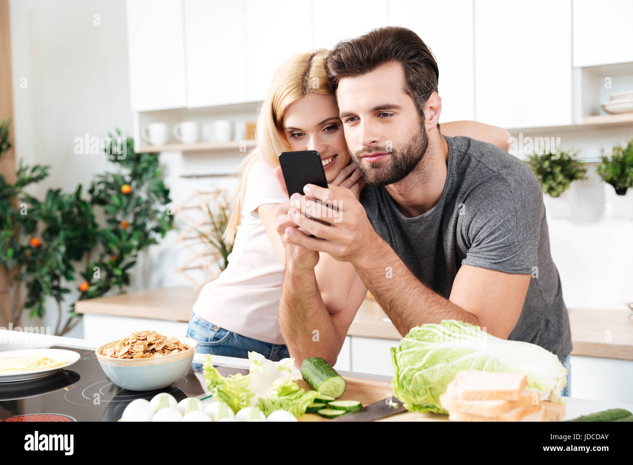 Happy couple using mobile phone to find a recipe for cooking while ...