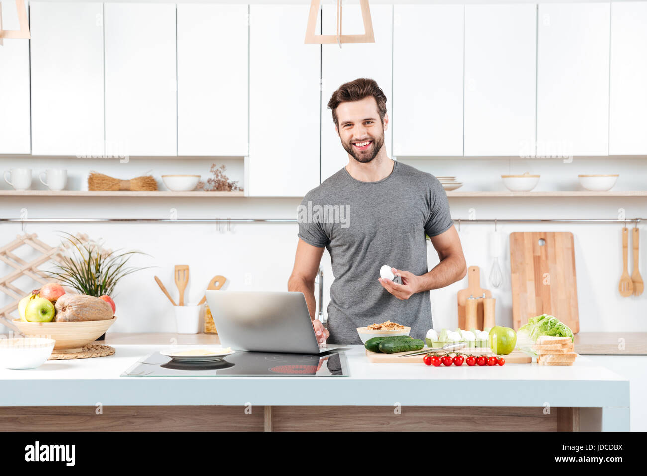 Attractive young man cooking with mixing bowl and looking at camera in ...