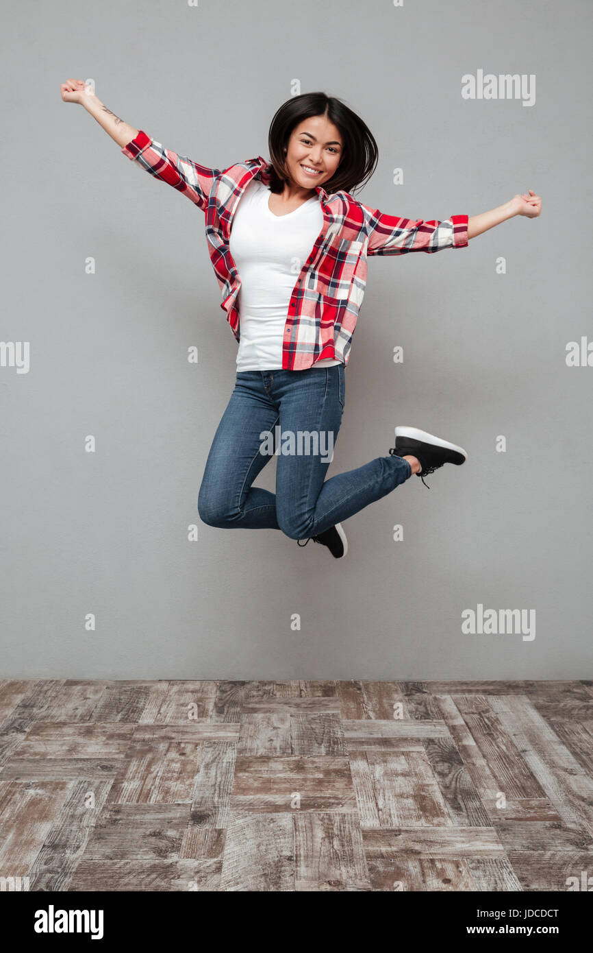 Photo of young smiling woman jumping over grey wall. Looking at camera ...