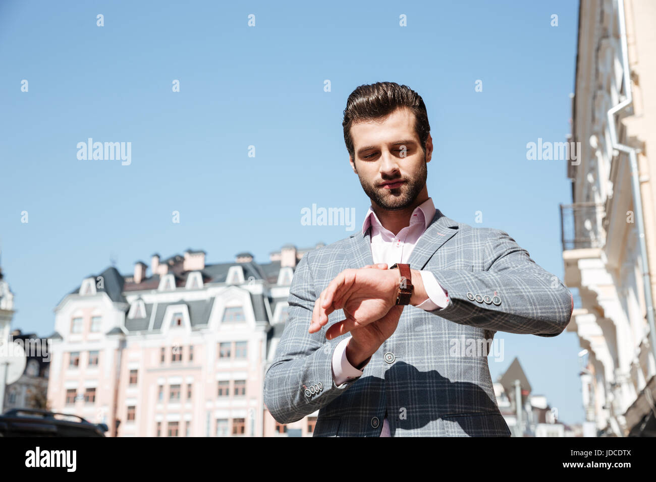 Portrait of a handsome young man checking the time on his wrist watch ...