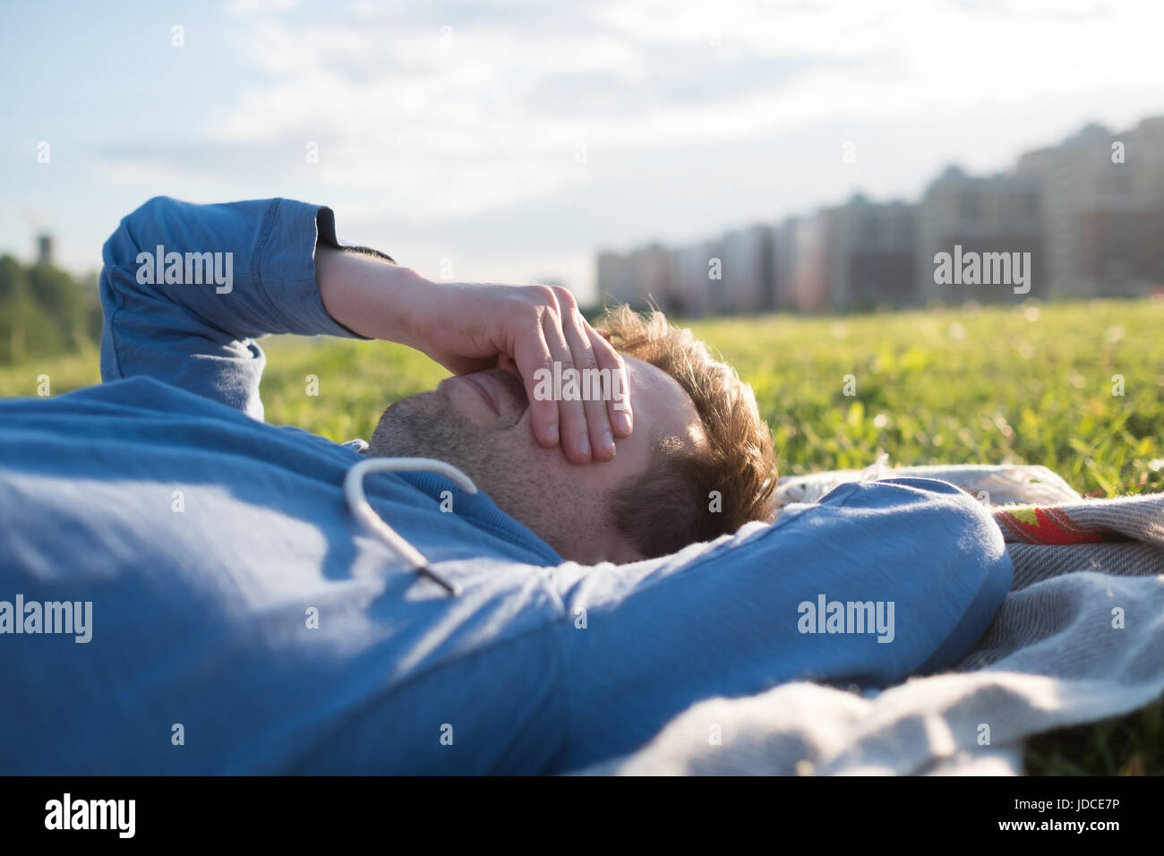 Sad tired man lying on the green grass with arms outstretched. City on ...