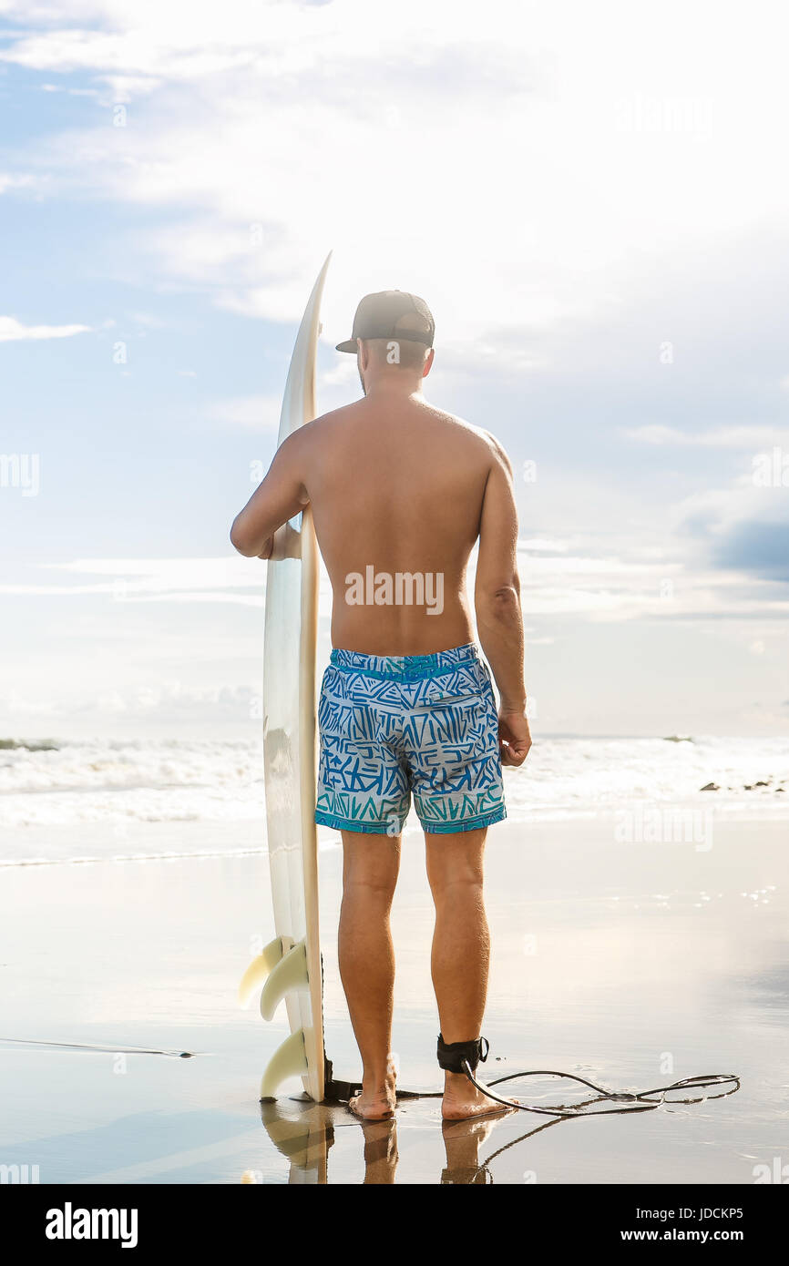Close up of handsome man stand with surfing board at surf spot at sea ...