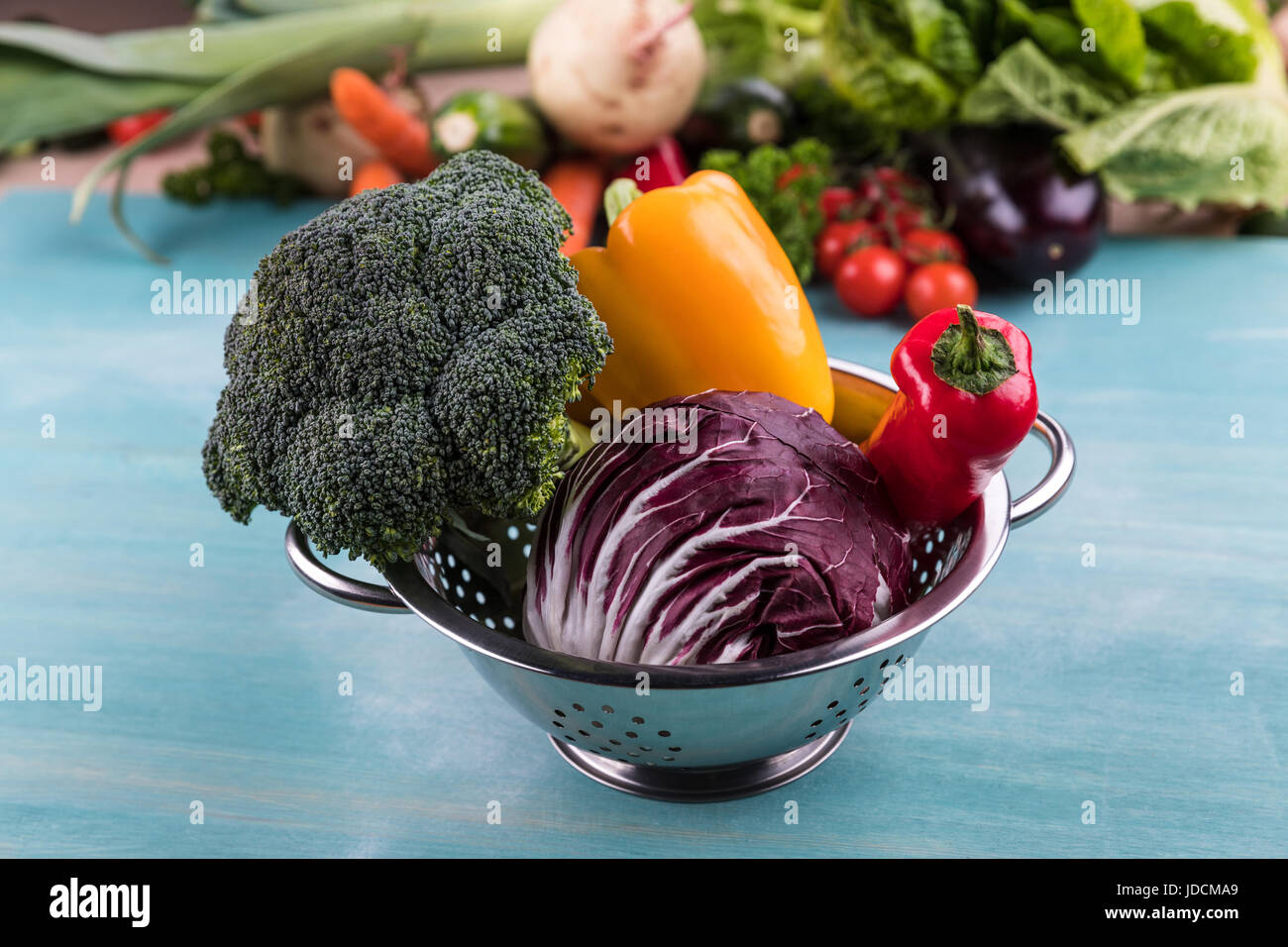 different fresh seasonal vegetables in colander on wooden table ...