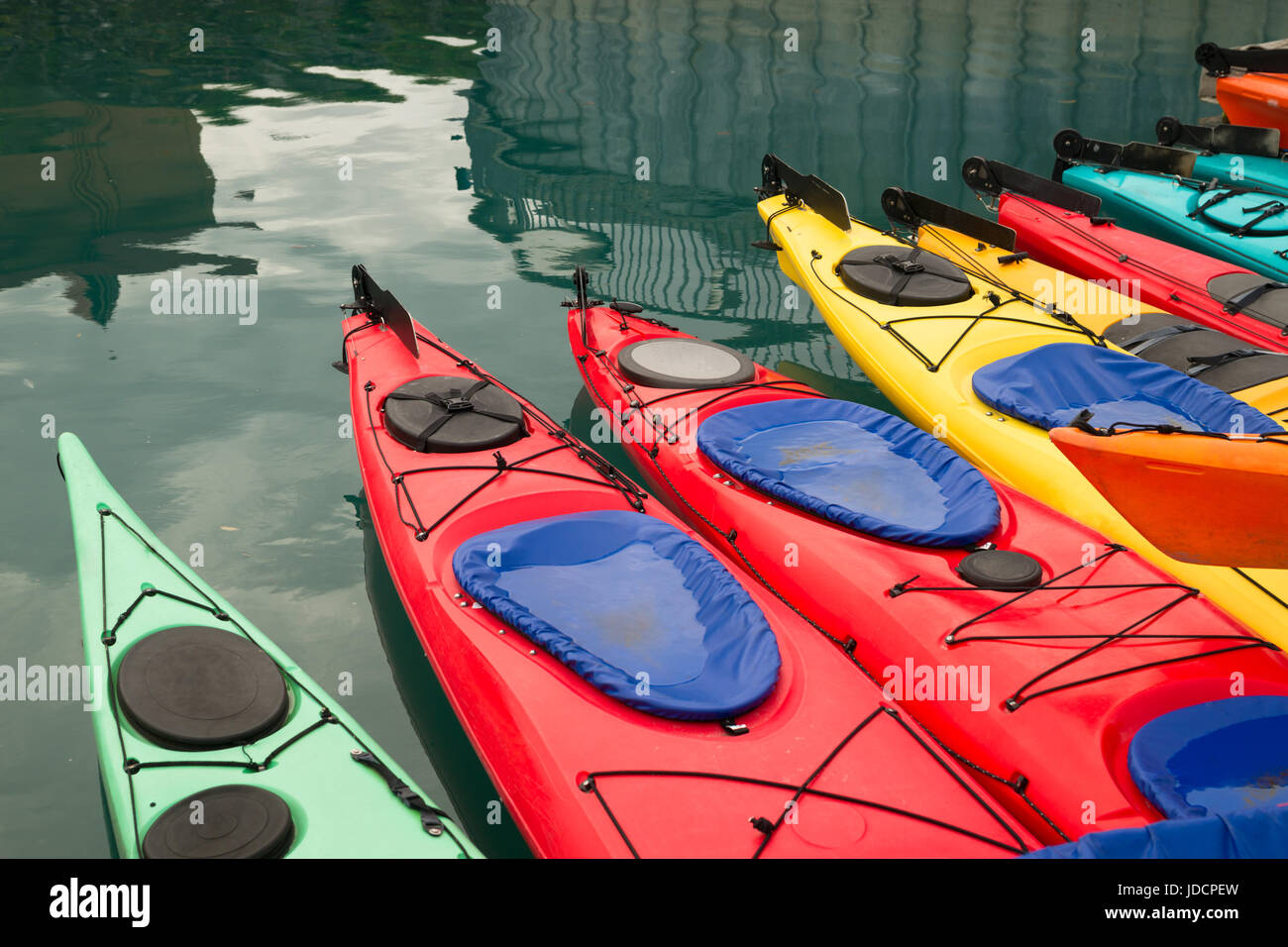 Red Teal Yellow and Orange Kayaks float on water of teal color Stock ...