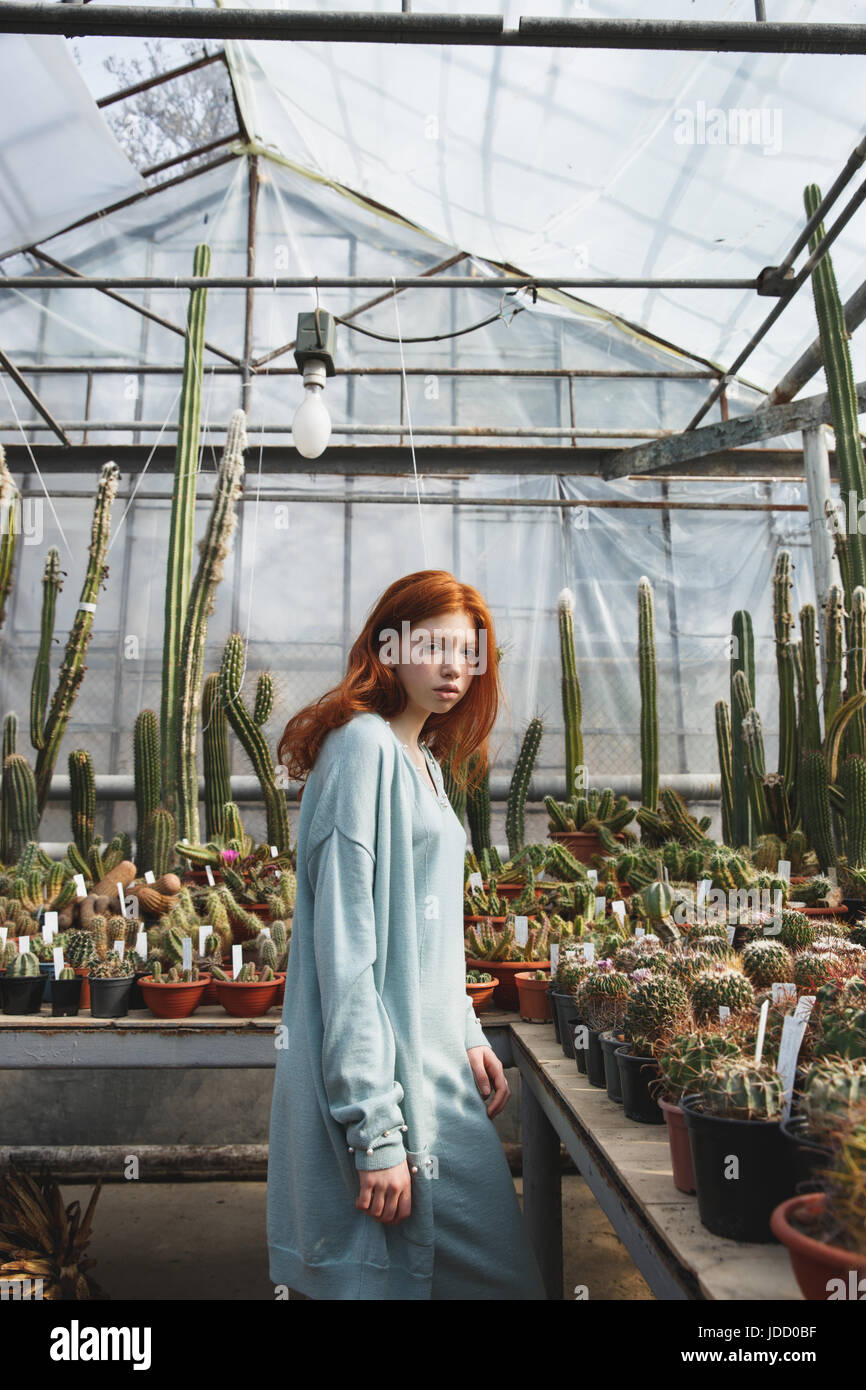 Portrait of a young redheaded girl standing in a glass house and ...