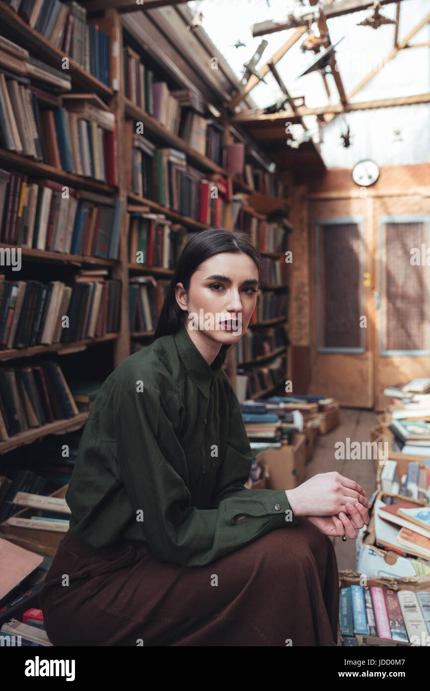 Portrait of beautiful girl in library looking camera while sitting on ...