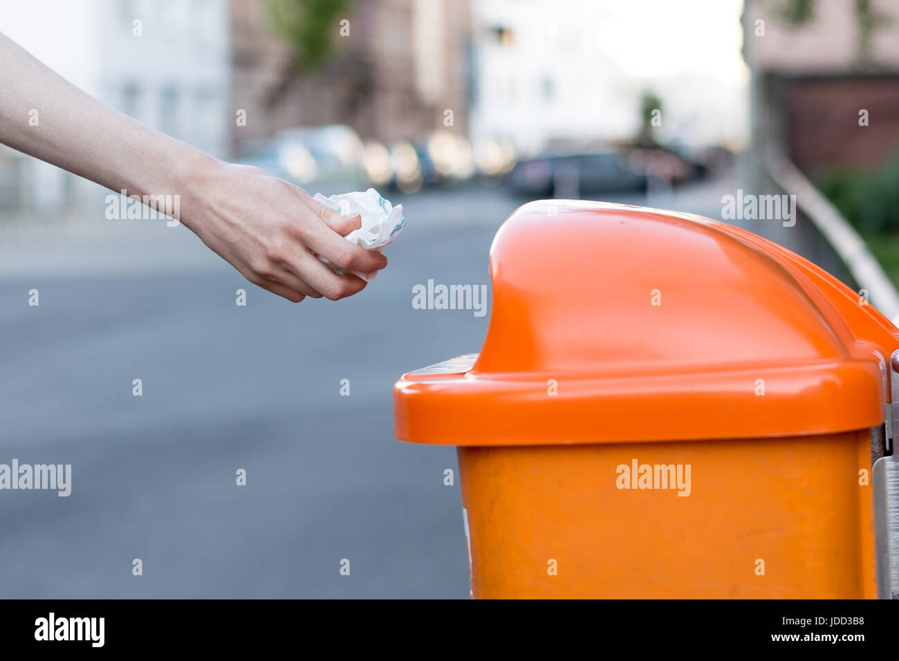 Throwing waste into a an orange trash can in the street from the side ...
