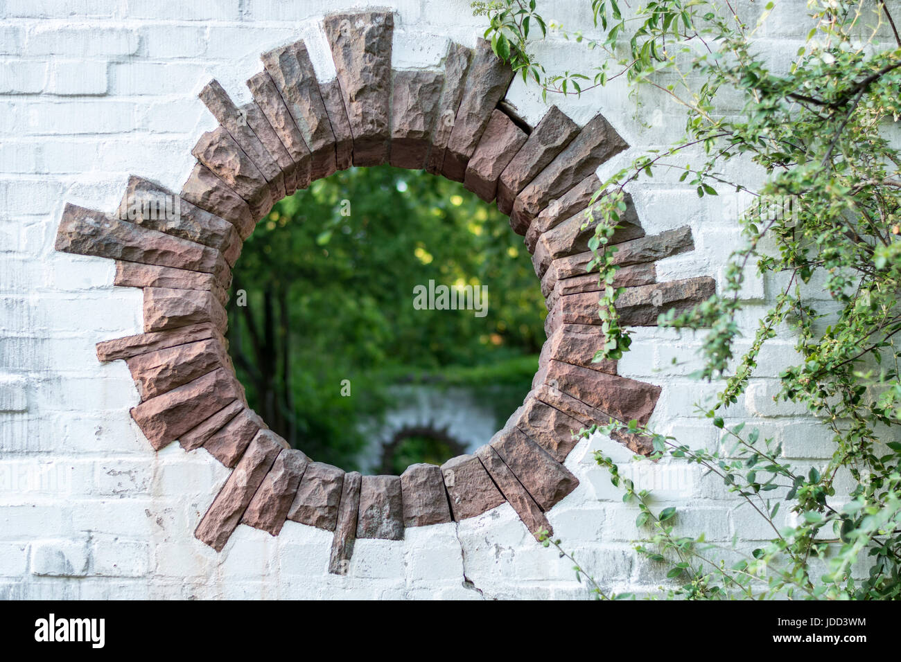 A round hole in a brick wall in a park looks like a portal to another ...