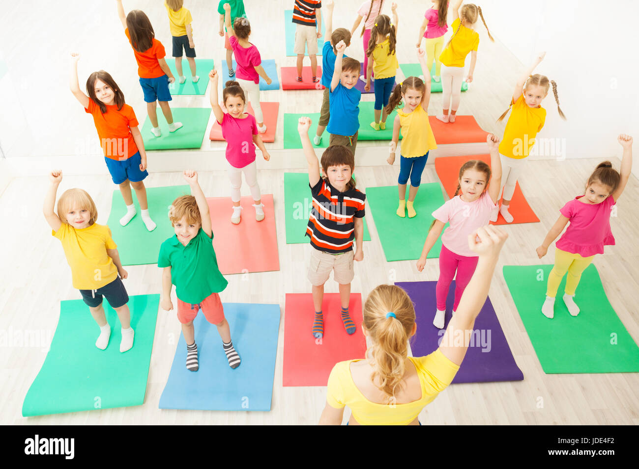 Group of age-diverse kids in sportswear standing on mats with arms ...