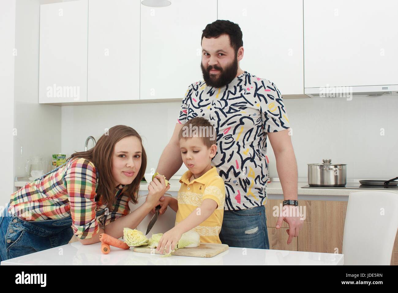 family of three eating fruits and vegetables in the kitchen, happy ...