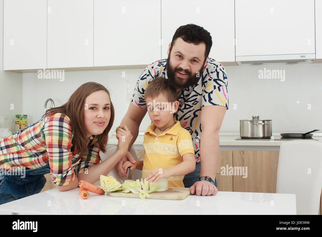 family of three eating fruits and vegetables in the kitchen, happy ...